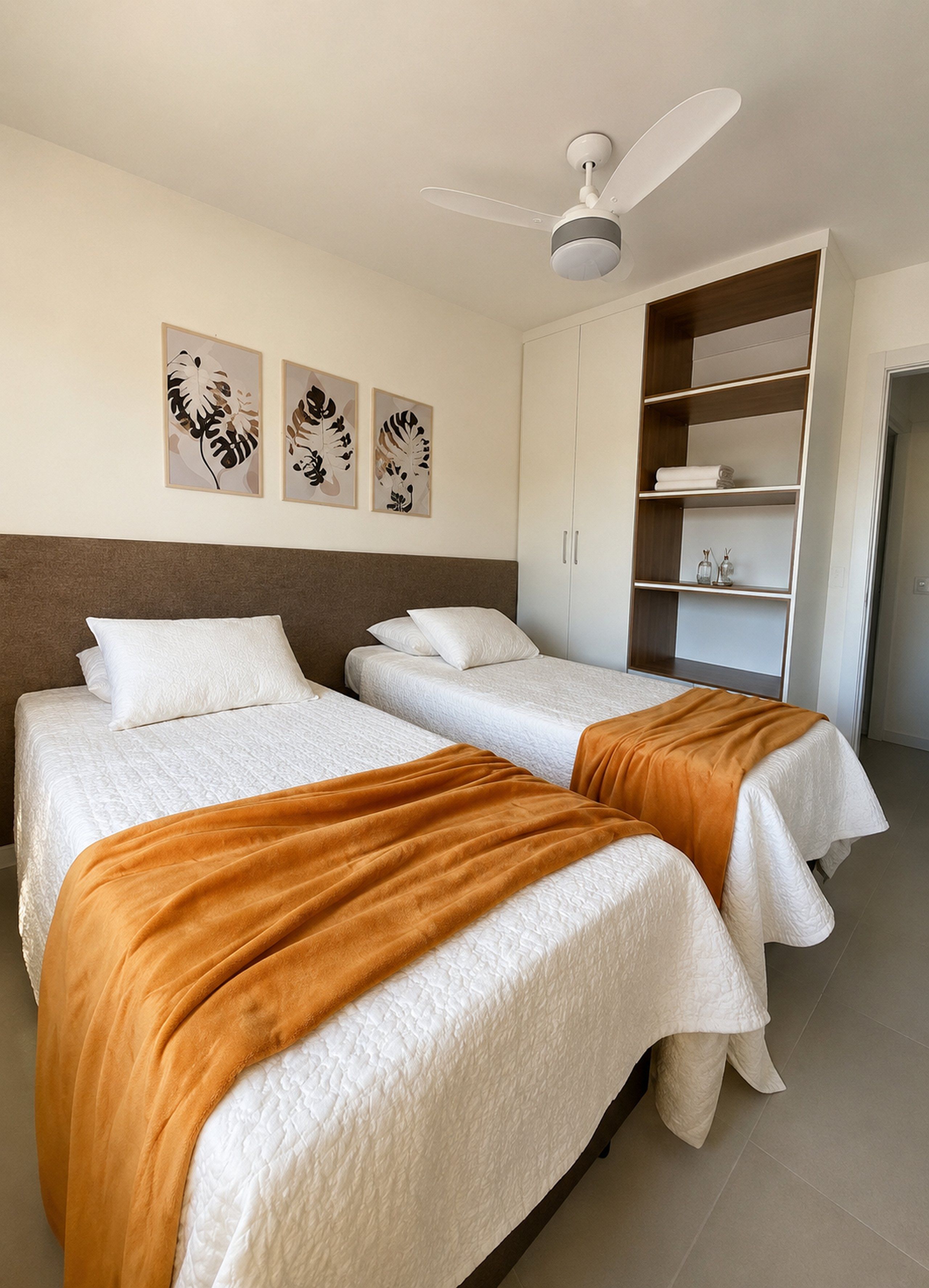 Quarto de hotel com duas camas, um ventilador de teto e um guarda-roupa com prateleiras.