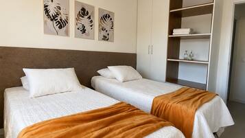 Quarto de hotel com duas camas, um ventilador de teto e um guarda-roupa com prateleiras.