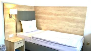 Uma cama de solteiro com cabeceira de madeira e mesa de cabeceira com abajur.