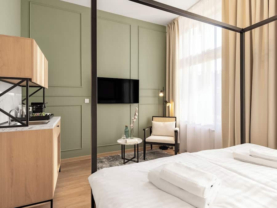 Quarto de hotel com cama, escrivaninha, televisão de tela plana, cadeira e pequena mesa com abajur.