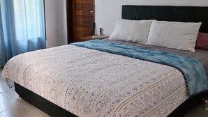 Quarto com cama, porta de madeira, mesa de cabeceira e janela com cortinas.