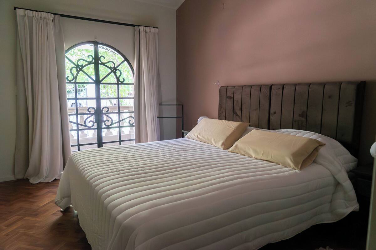 Quarto com uma cama grande, cabeceira de madeira e janela com cortinas.