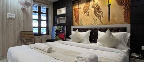 Cama bem arrumada com lençóis brancos, uma obra de arte na parede e uma mesa de cabeceira com abajur.