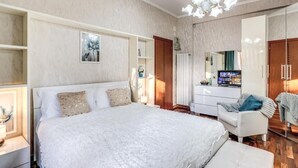 Quarto com uma cama grande, uma cadeira branca, cômoda e um espelho.
