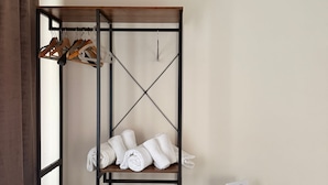 Quarto com armário de madeira contendo toalhas dobradas e uma pequena mesa com um dispositivo preto.