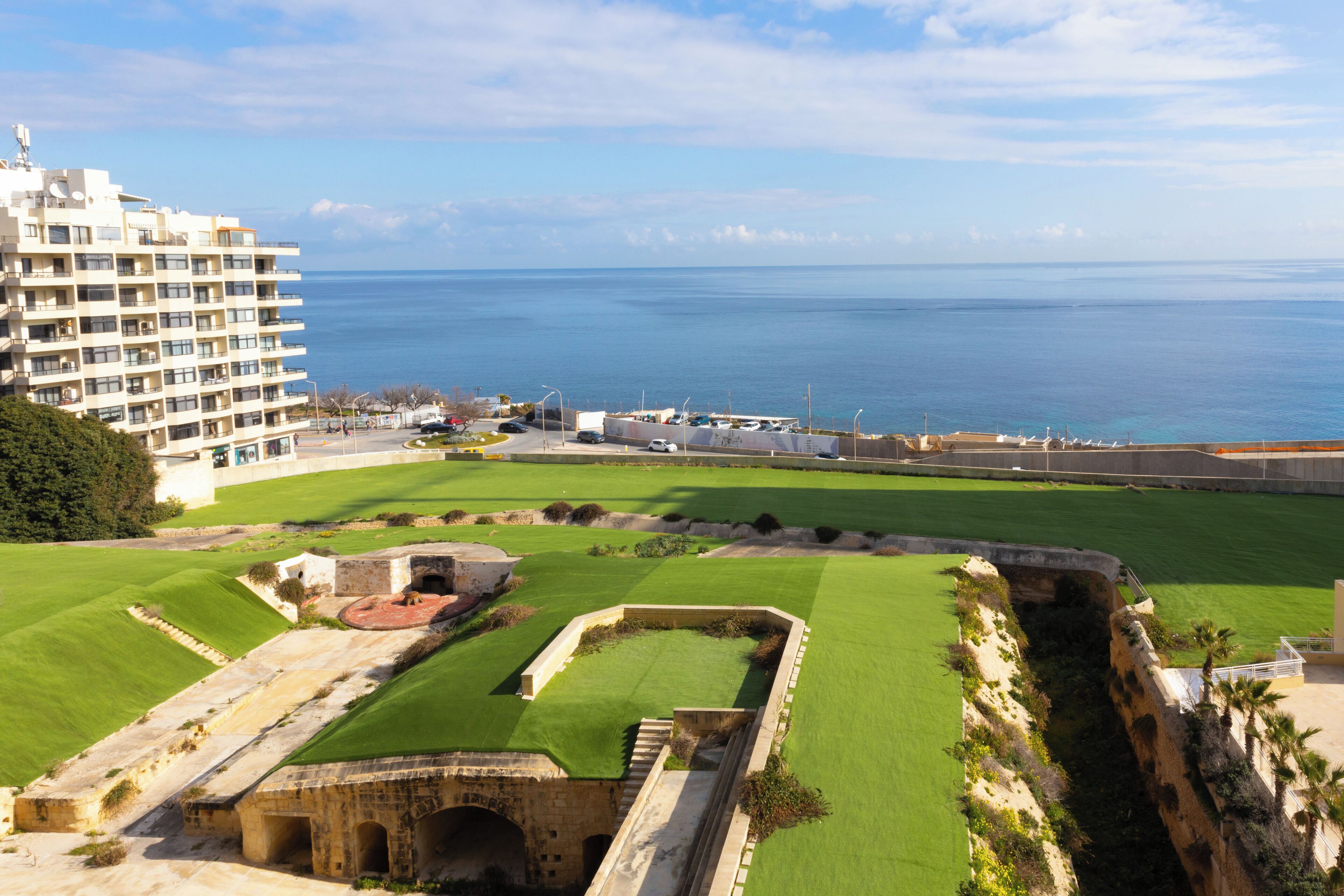 Um hotel à beira-mar com vista para o mar, um gramado bem cuidado e uma fortificação histórica.