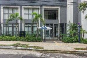 Um edifício moderno com entrada de vidro, um guarda-chuva azul e palmeiras.