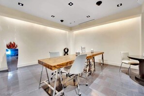 Uma sala de conferências com uma longa mesa de madeira, cadeiras brancas e uma mesa redonda escura.