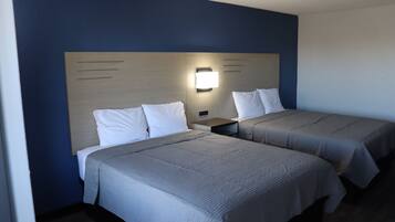 Quarto de hotel com duas camas, uma mesa de cabeceira e uma luminária fixada na parede.