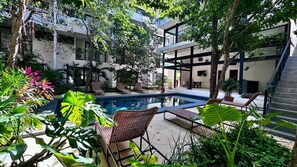 Uma área de piscina moderna ao ar livre com um nível superior envidraçado, rodeada por plantas tropicais exuberantes e áreas de estar.