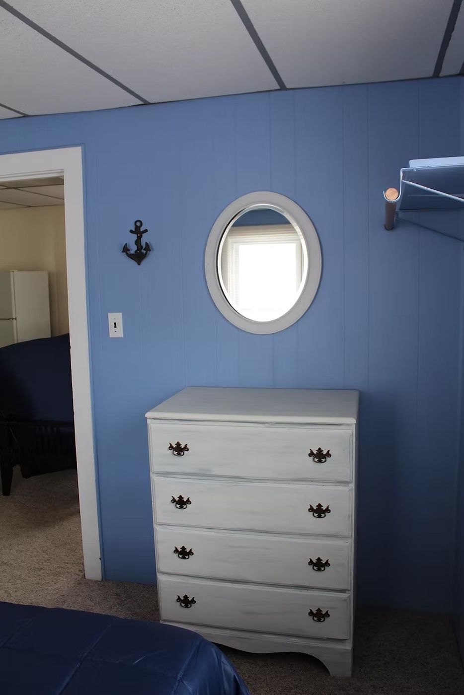 Quarto com penteadeira branca, espelho redondo e parede azul.