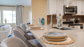 Uma cozinha moderna com ilha central, eletrodomésticos de aço inoxidável e um espaço de refeições com sofá e cadeiras.
