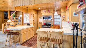 Interior de uma cabana de madeira com cozinha, banquetas de madeira e uma mesa de jantar.