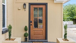 Um edifício bege com uma porta marrom, número 5, e dois pequenos vasos de plantas de ambos os lados.