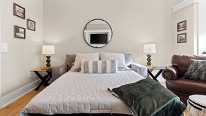 Quarto com uma cama grande, duas mesas de cabeceira com luminárias, um sofá de couro marrom e um espelho redondo na parede.