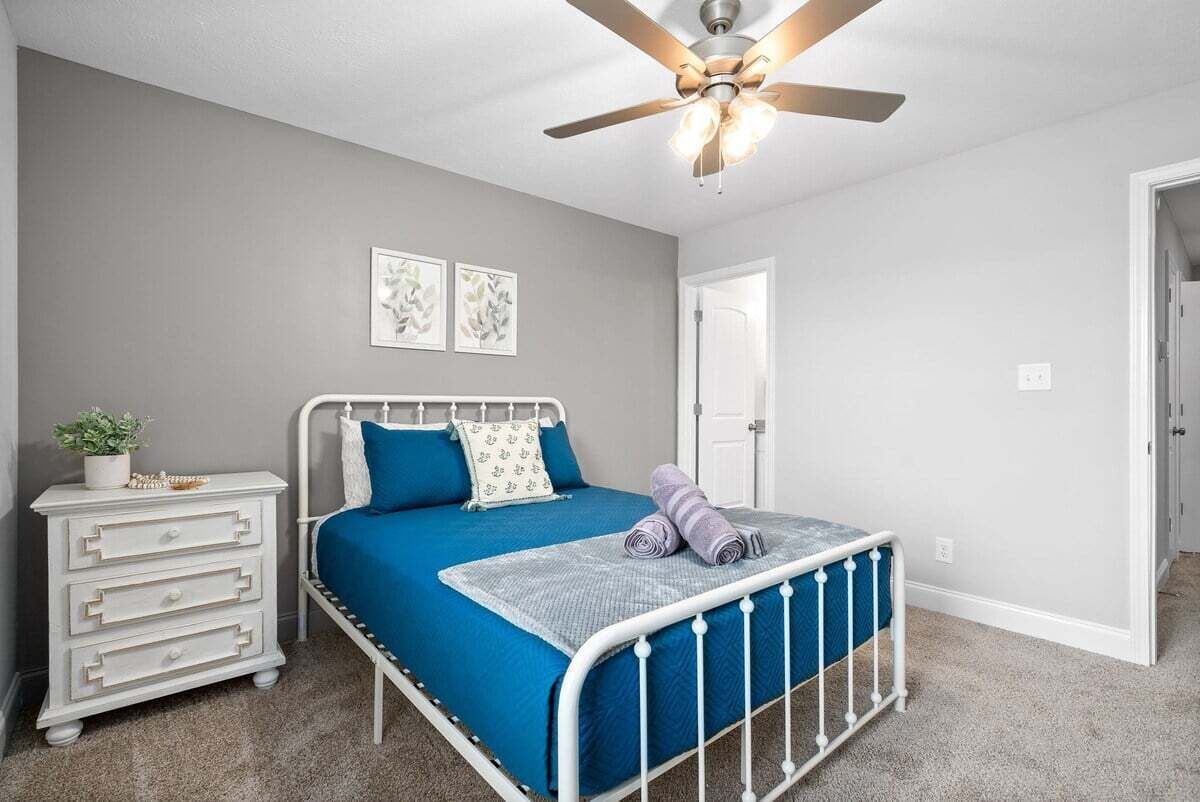 Quarto com cama, penteadeira, ventilador de teto e duas obras de arte nas paredes.