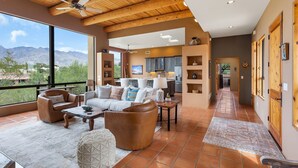 Uma sala de estar ampla com uma grande janela, teto de madeira e vista para as montanhas.