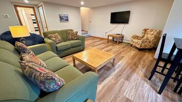 Uma sala de estar com um sofá verde, uma mesa de centro de madeira e uma poltrona estampada.
