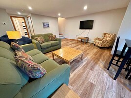 Uma sala de estar com um sofá verde, uma mesa de centro de madeira e uma poltrona estampada.