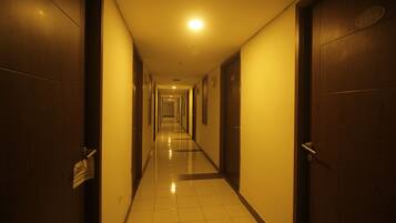 Corredor de hotel com portas em ambos os lados, chão de azulejos e iluminação no teto.