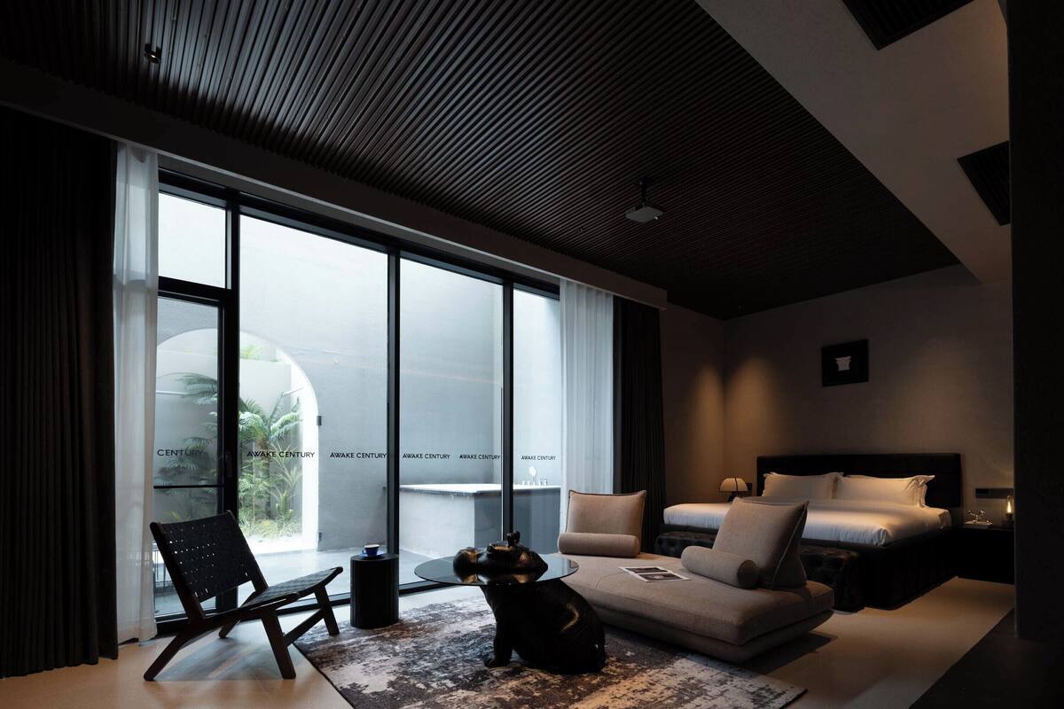 Quarto de hotel moderno com uma grande janela, um sofá, uma cama e uma pequena mesa.