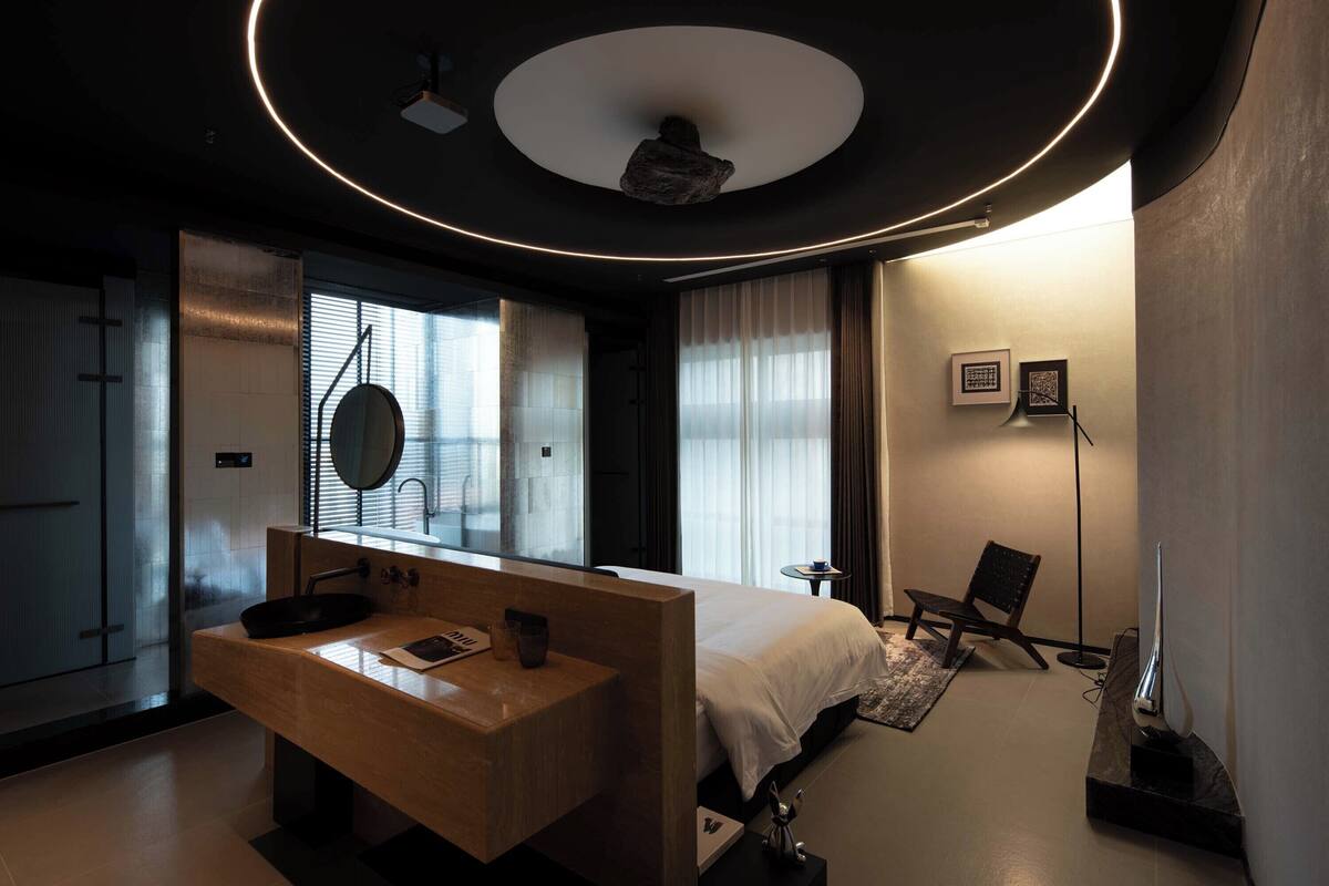 Quarto de hotel moderno com toucador de madeira, uma cama grande, área de estar com uma cadeira e uma escrivaninha.