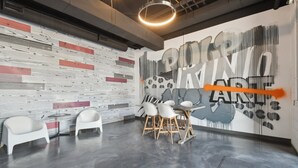 Um espaço de escritório moderno com um grande mural na parede, cadeiras brancas, uma mesa redonda e um lustre.