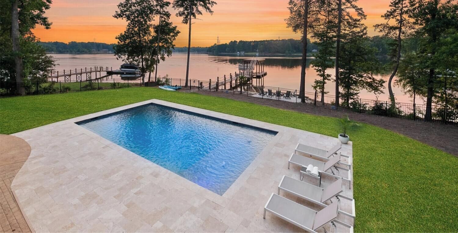 Piscina retangular com um deck, rodeada por um gramado e um píer de madeira que se estende para um lago.