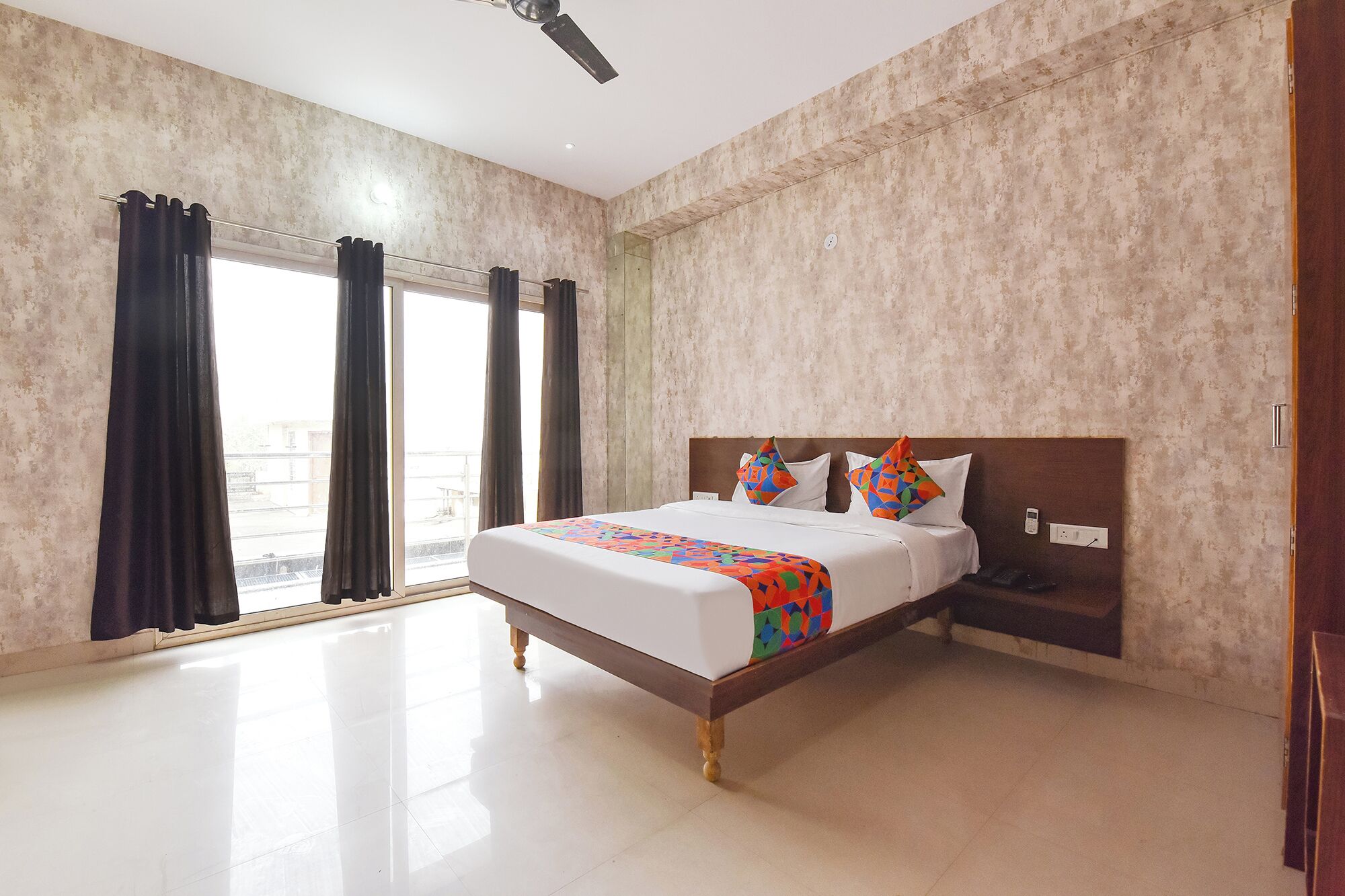 Quarto de hotel com uma cama grande, mesa de cabeceira, ventoinha no teto e vista pela janela.