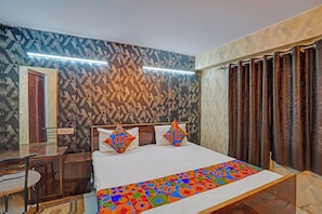 Um quarto com parede de padrão geométrico, uma cama com almofadas coloridas e uma mesinha de cabeceira.