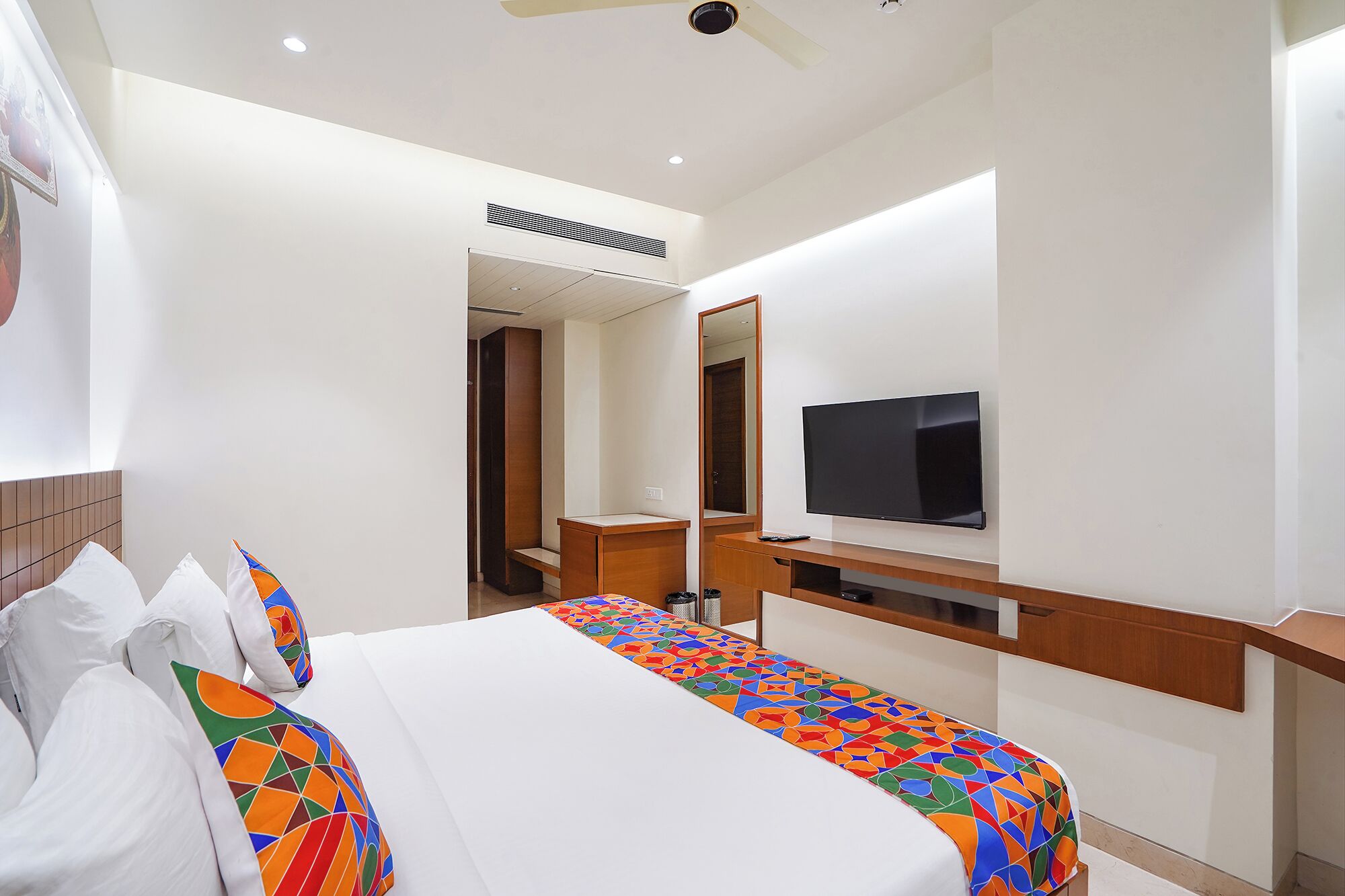 Quarto de hotel com cama, televisão, escrivaninha e espelho.