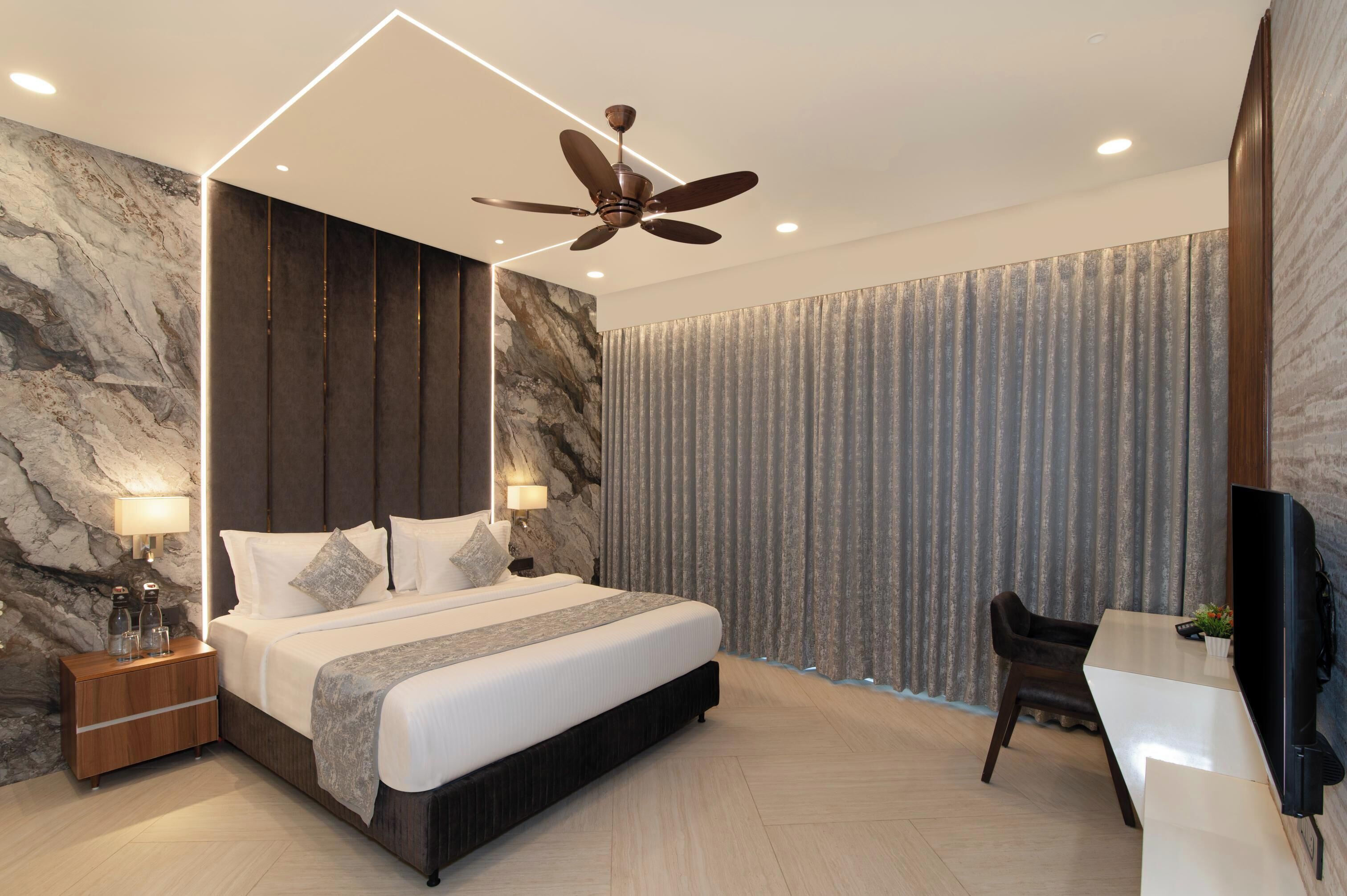 Quarto de hotel moderno com uma cama grande, uma escrivaninha, um ventilador de teto e uma televisão.