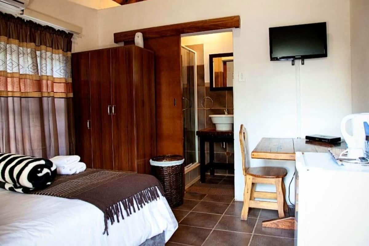 Quarto de hotel com cama, escrivaninha, cadeira, televisão e banheiro com chuveiro.