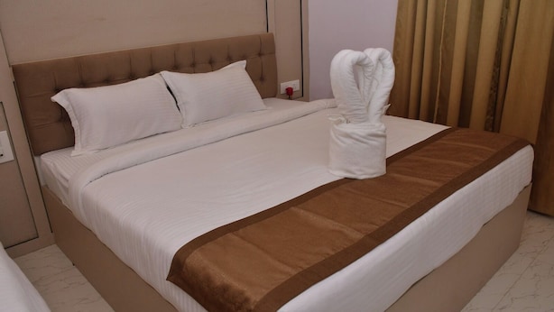 Cama bem arrumada com lençóis brancos, um manta marrom de destaque e uma toalha dobrada sobre a cama.