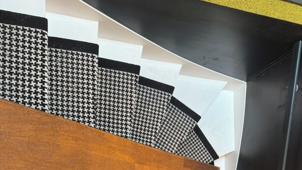 Escadaria em espiral com corrimão de madeira e degraus com padrão preto e branco.