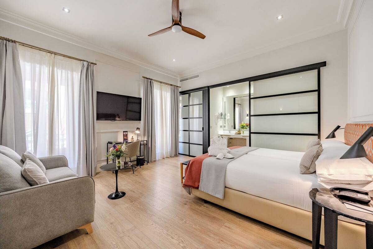 Quarto de hotel moderno com cama, sofá, escrivaninha e televisão.