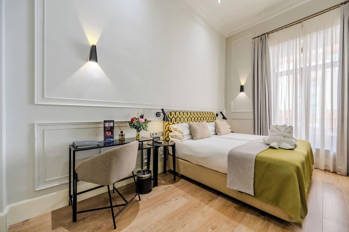 Quarto bem organizado com cama, mesa de cabeceira, cadeira e escrivaninha com abajur.