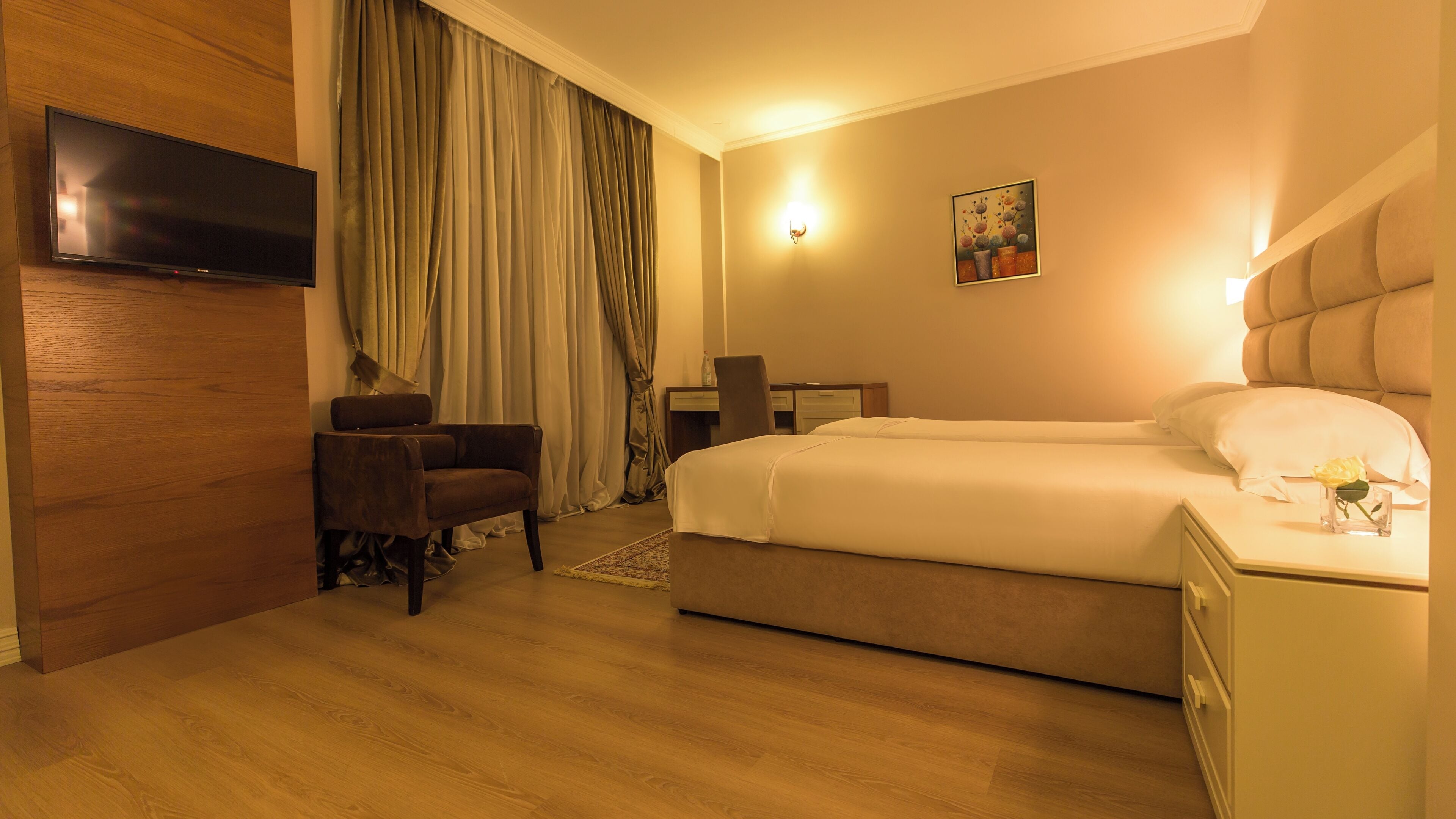 Quarto de hotel com cama, escrivaninha, cadeira, televisão e um quadro na parede.