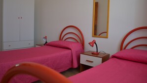 Quarto com duas camas, guarda-roupa, espelho e escrivaninha com abajur.