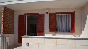 Fachada de edifício com duas persianas vermelhas abertas, parede de tijolos e entrada com azulejos.