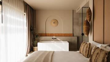Quarto de hotel moderno com uma cama grande, uma banheira integrada e uma janela ampla com cortinas.