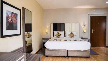 Quarto de hotel com uma cama grande, mesas de cabeceira, um espelho e um quadro na parede.