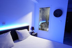 Quarto moderno com cama, mesa de cabeceira, abajur e relógio na parede.