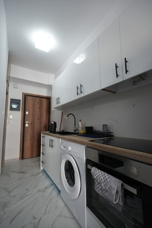 Uma cozinha compacta com armários brancos, máquina de lavar e forno embutido.