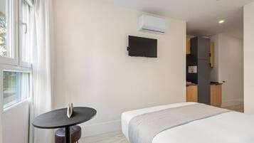 Quarto de hotel moderno com uma cama, uma mesa redonda pequena, uma TV de tela plana na parede e um aparelho de ar condicionado.