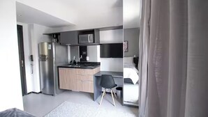 Quarto de hotel moderno e compacto, com cozinha compacta, cama e escrivaninha.