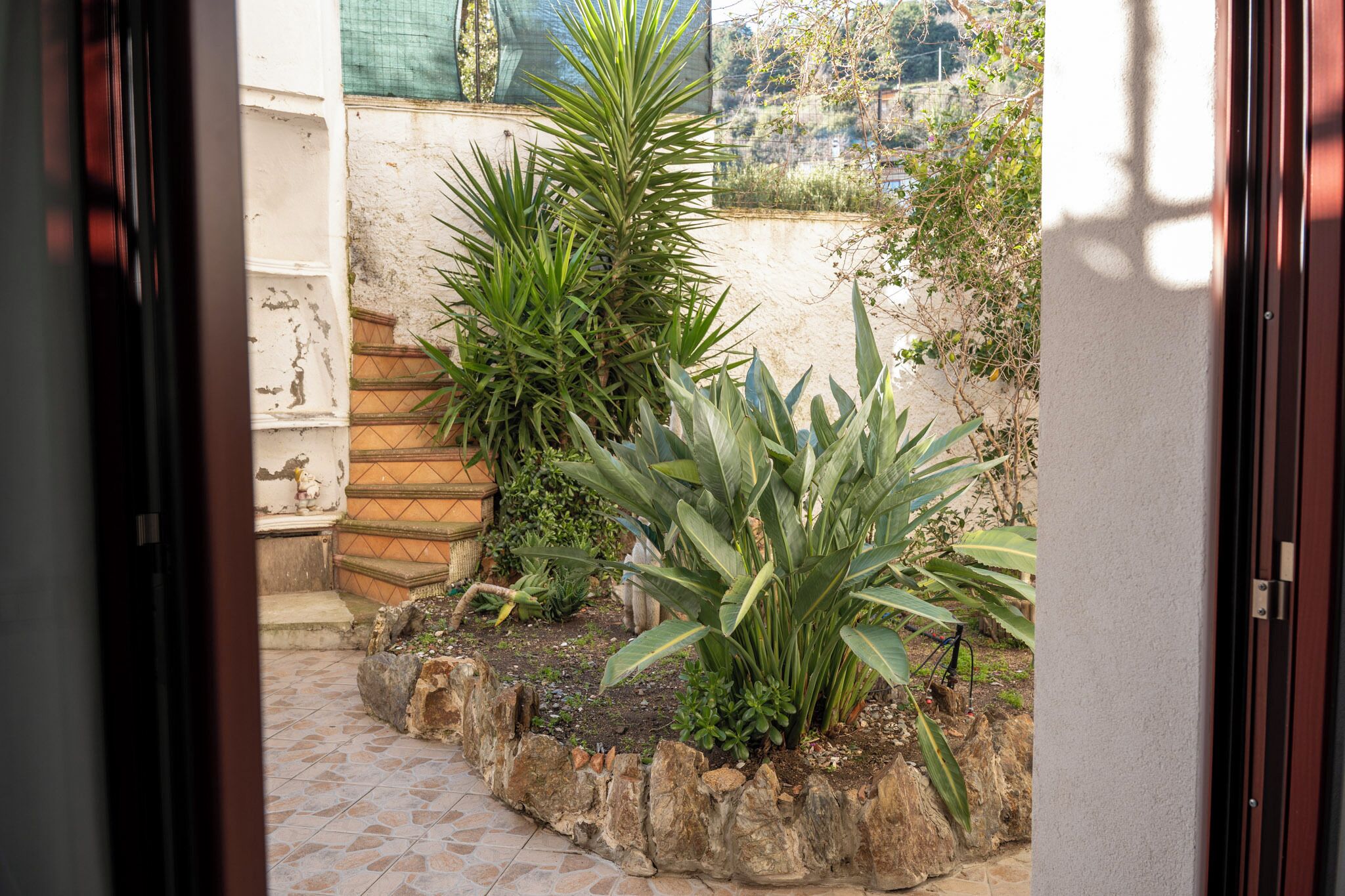 Um pátio com caminho de pedra, plantas em vasos e escadaria para um nível superior.