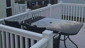 Um terraço com mesa e cadeiras, com vista para uma área residencial com casas e o mar ao longe.