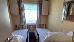 Quarto com duas camas, uma mesinha com abajur e uma janela com cortinas.