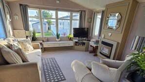Sala de estar com sofá, televisão, lareira e vista para as casas lá fora.